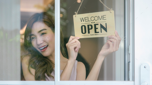 Woman store owner turning open sign broad through the door glass and ...