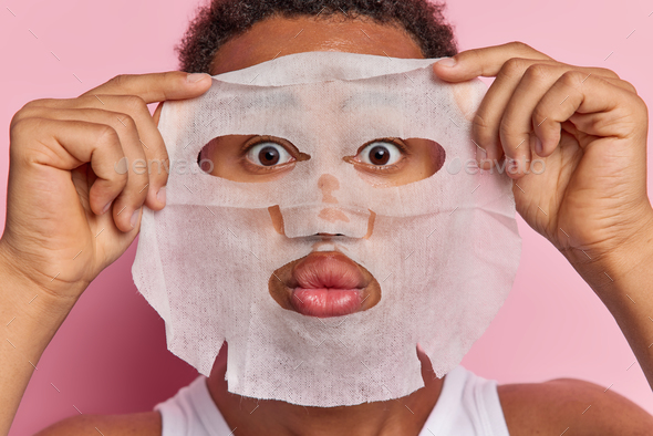 Stunned young man keeps beauty sheet mask over face stares stupefied ...