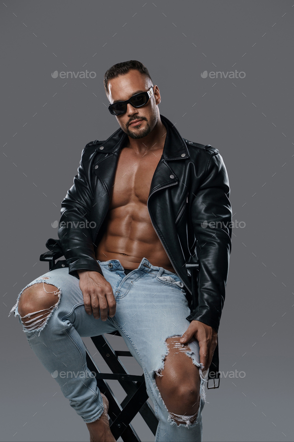 Handsome male model seated on a studio chair against grey backdrop ...