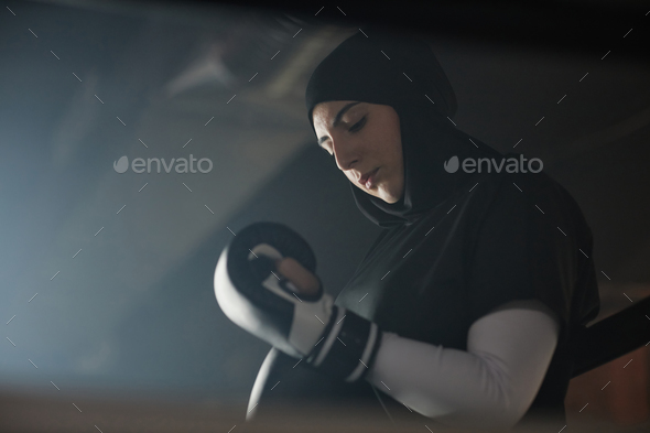 Young Muslim female boxer in hijab putting on boxing gloves before ...