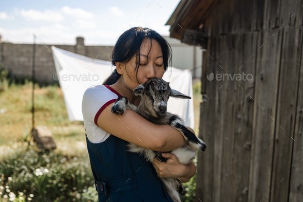 Farmer asian woman holding baby goat in her arms on a farm. Stock Photo ...