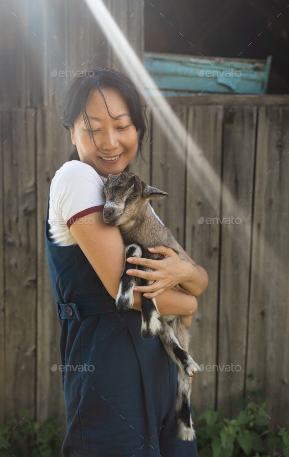 Farmer asian woman holding baby goat in her arms on a farm. Stock Photo ...