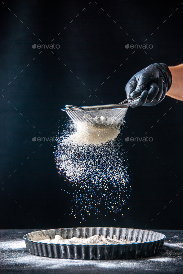 front view female cook pouring white flour into the pan on the dark ...
