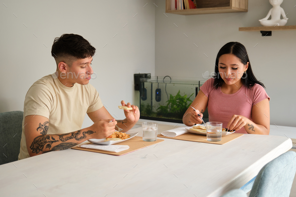 Two young latin people eating traditional arepas in the living room ...