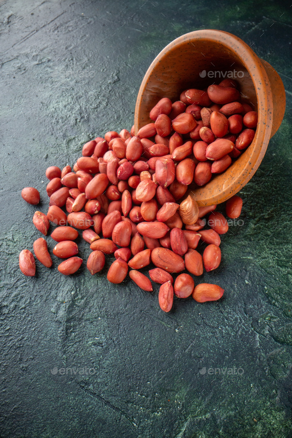 Front view of red peanuts fallen from brown pot on blue and black ...