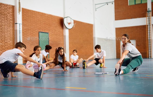 Group of school kids exercising with their sports teacher during ...