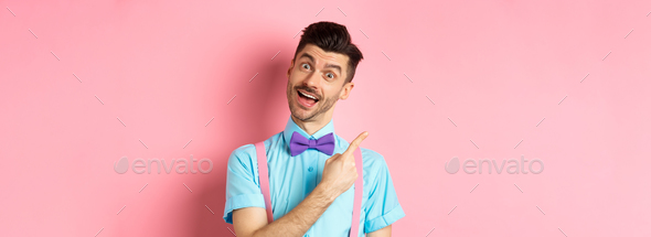Funny male model in bow-tie, tilt head and pointing finger left ...