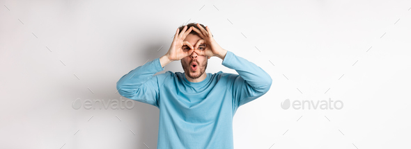 Check it out. Impressed young man seeing awesome promo, looking through ...