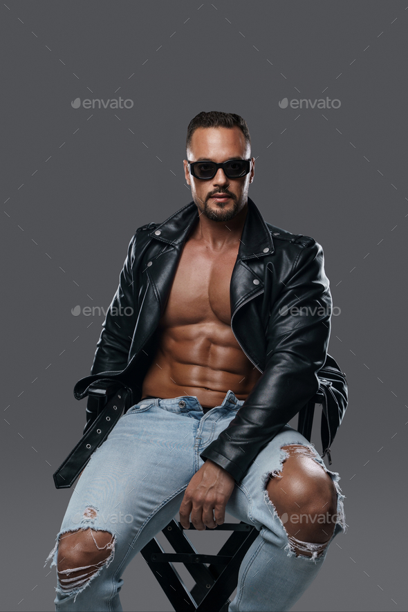 Handsome male model seated on a studio chair against grey backdrop ...