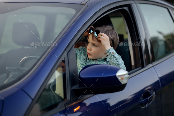 The boy sits behind the wheel of his father's car in sunglasses and ...