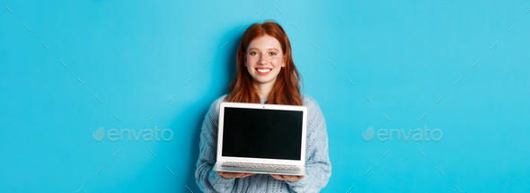 Young smiling woman with red hair and freckles showing computer screen ...