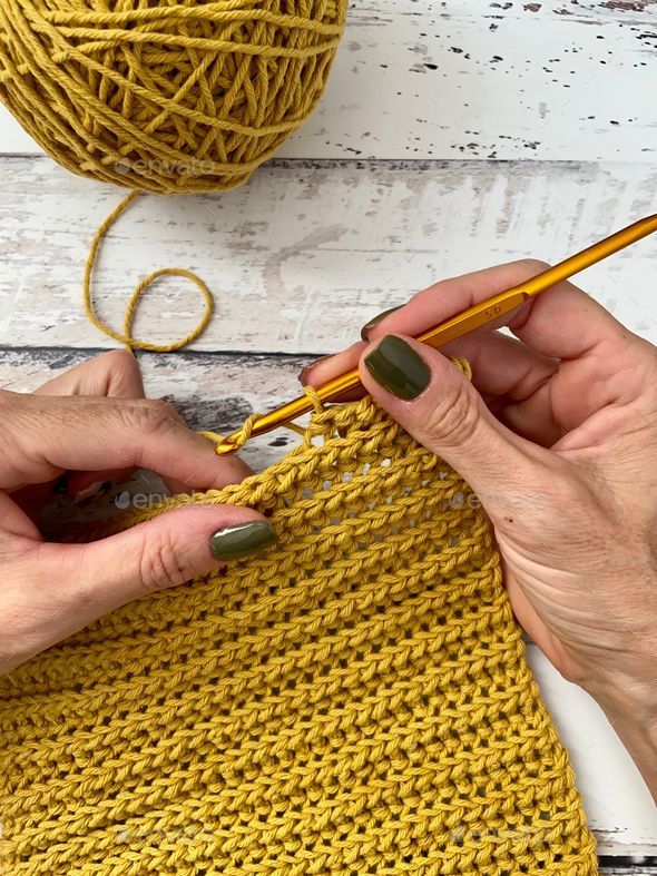 Females hands crocheting with a yellow yarn with a wooden surface in ...