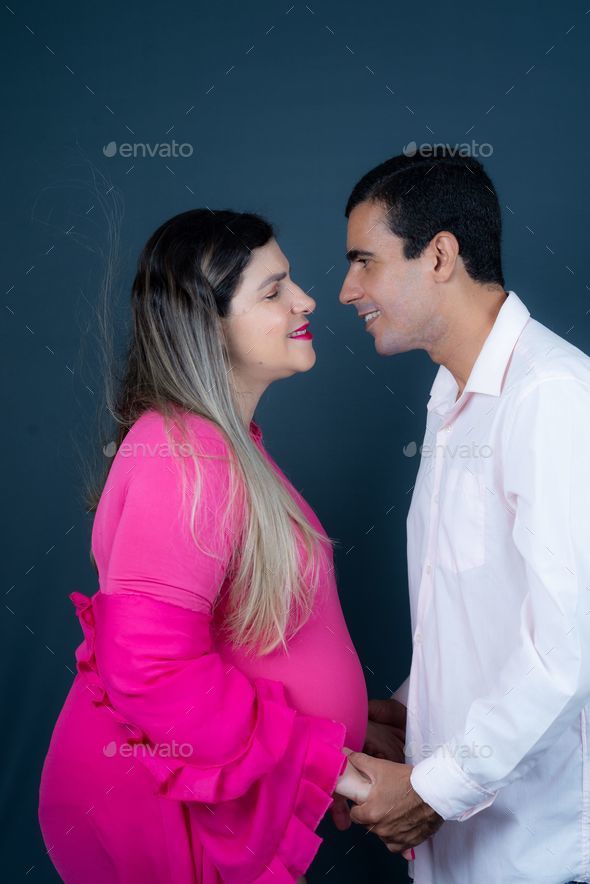 Loving couple, both with visible baby bumps, embrace each other against ...