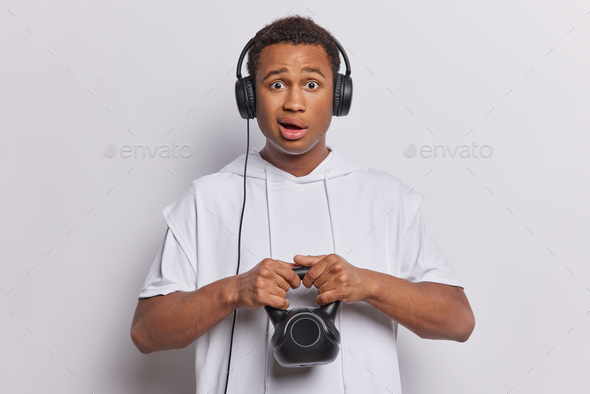 Puzzled dark skinned man holds weight displaying his sculpted muscles ...