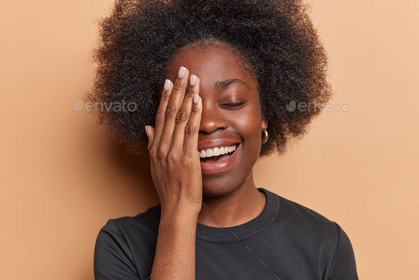 Joyful dark skinned woman makes face palm smiles broadly keeps eyes ...