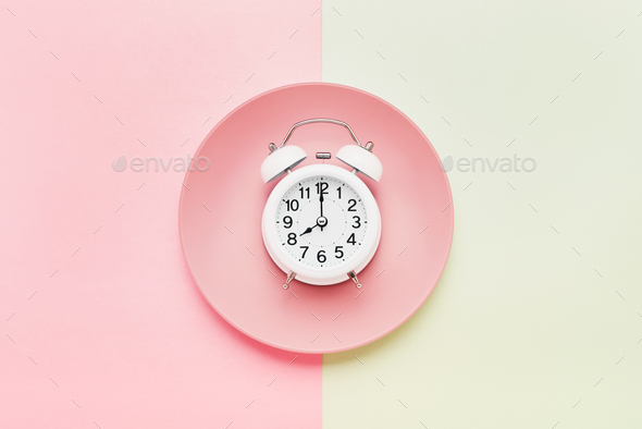 Intermittent fasting concept. White alarm clock on empty pink plate ...