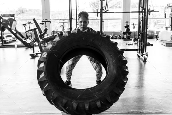 Woman performing tire flipping exercise in gym setting, showing ...