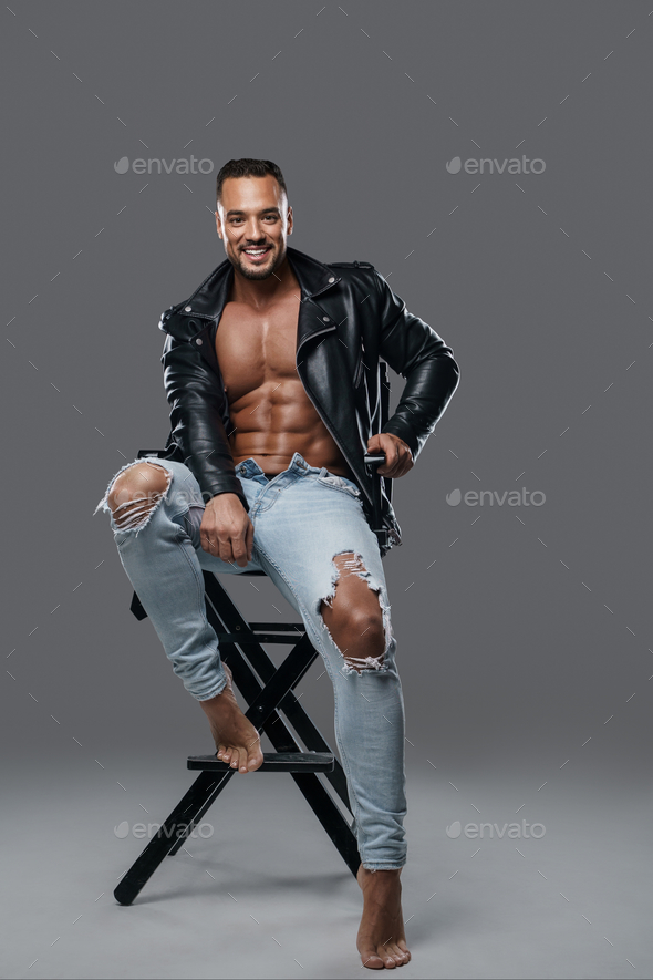 Handsome male model seated on a studio chair against grey backdrop ...