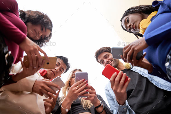 Multi-ethnic friends using their mobile phones while standing in a circle. Stock Photo by ...