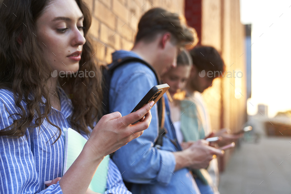 University students browsing phones next to university campus building ...