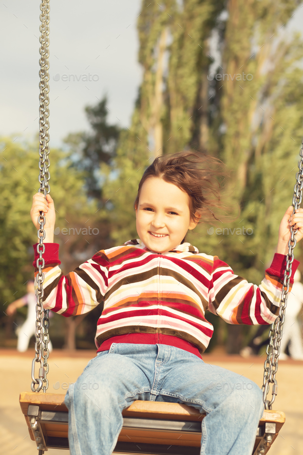 Smiling girl playing on a swing outdoor. Children summer activity ...