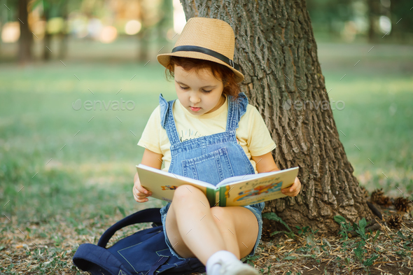 Little cute girl kid sitting under the tree on summer in the park ...