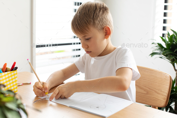 A cute boy makes a drawing with a ruler and pencil. Home lessons ...