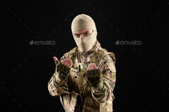 front view of young soldier in uniform and mask on black background ...