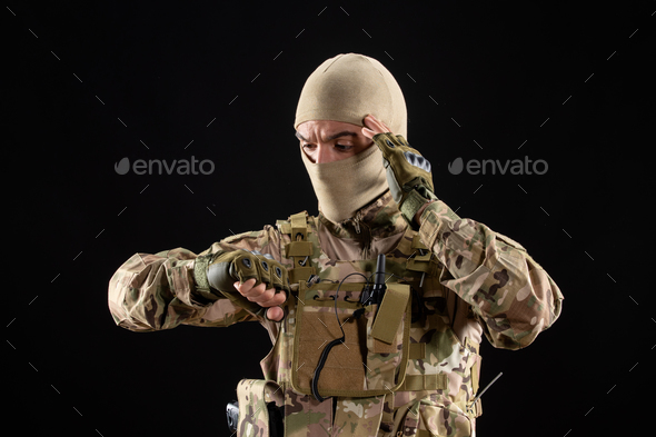 front view of young soldier in uniform checking time on black ...