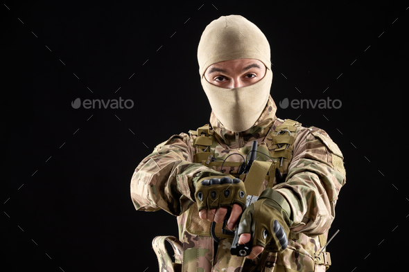 front view of young soldier in uniform reloading gun on black ...