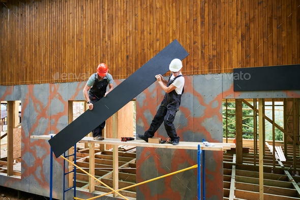 Workers cladding facade of house with cement particle boards while ...
