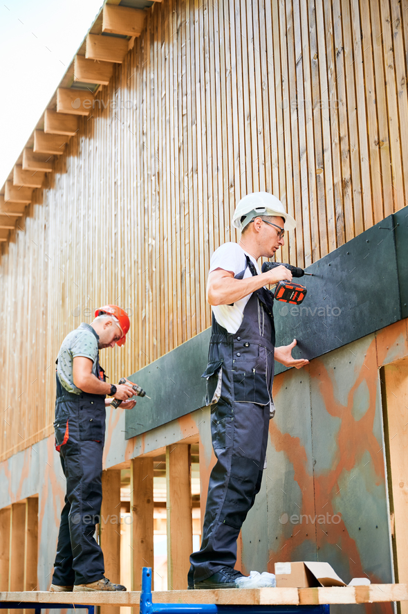 Workers cladding facade of house with cement particle boards while ...