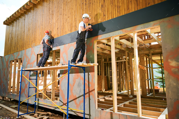 Workers cladding facade of house with cement particle boards while ...