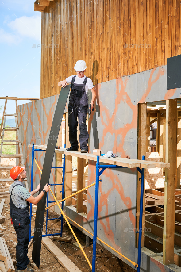 Workers cladding facade of house with cement particle boards while ...