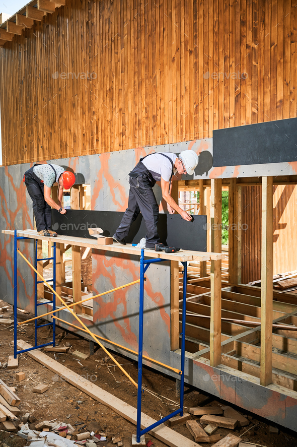 Workers cladding facade of house with cement particle boards while ...