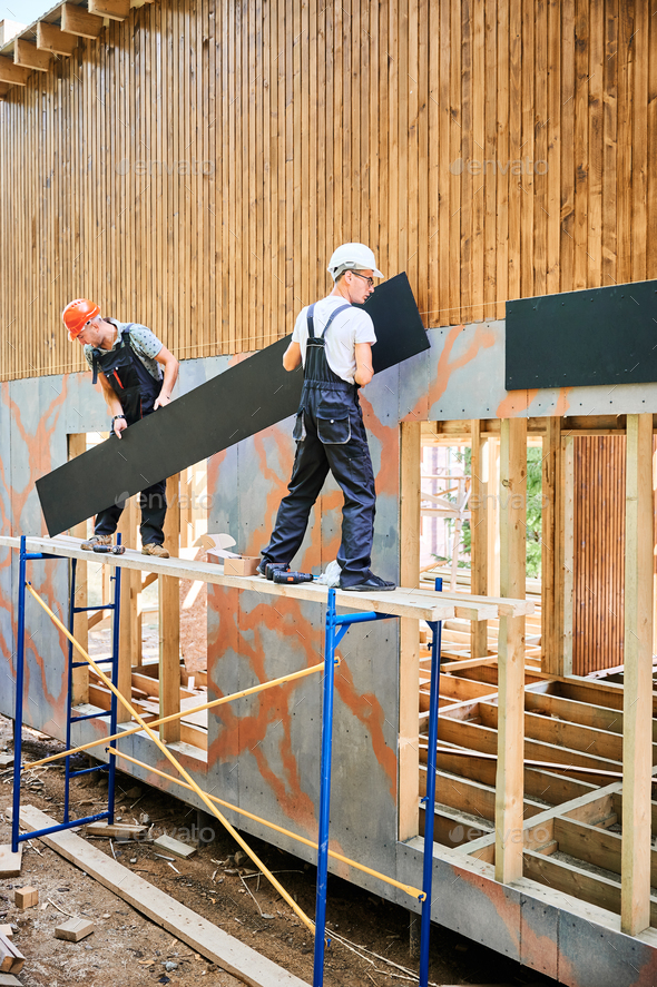 Workers cladding facade of house with cement particle boards while ...
