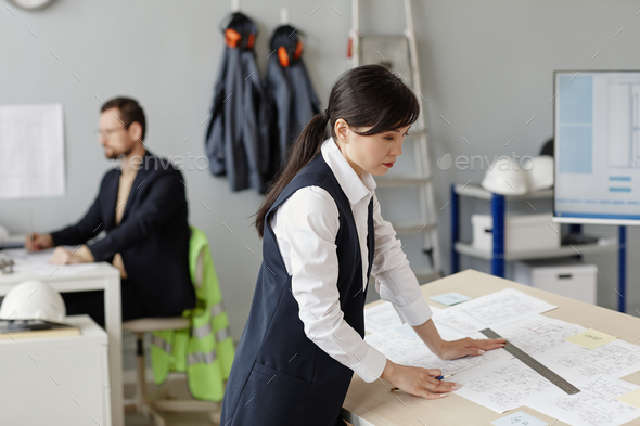 Asian woman as female engineer drawing blueprints and plans in office ...
