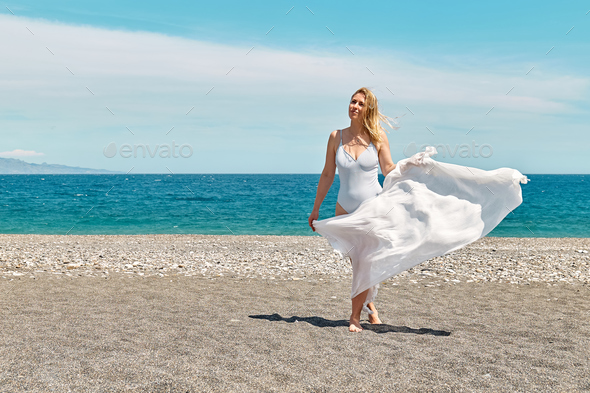 Pretty blond woman in swimsuit and white pareo enjoying sunny windy day ...