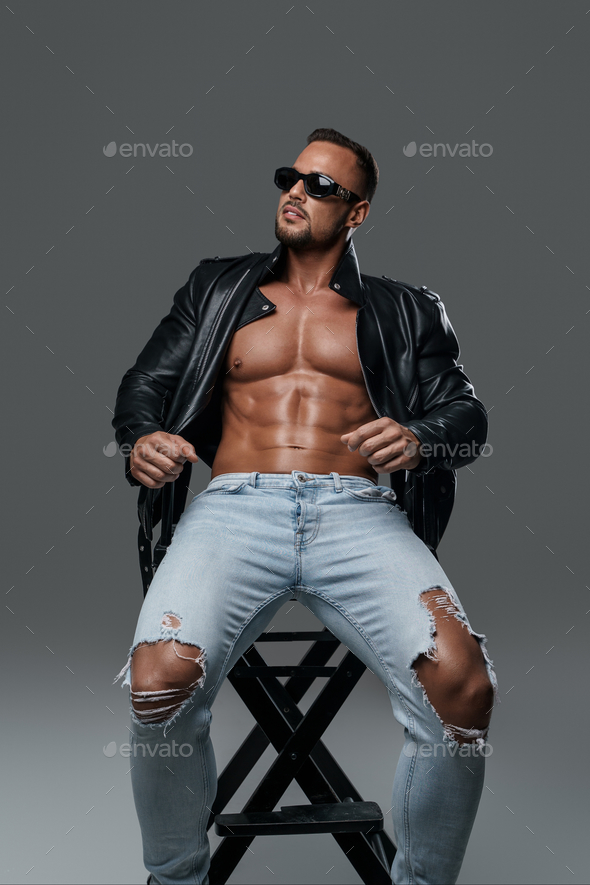 Handsome male model seated on a studio chair against grey backdrop ...