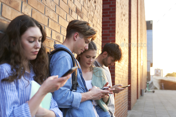 University students browsing phones next to university campus building ...