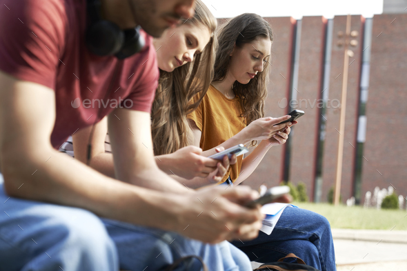 University students browsing phones next to university campus building ...