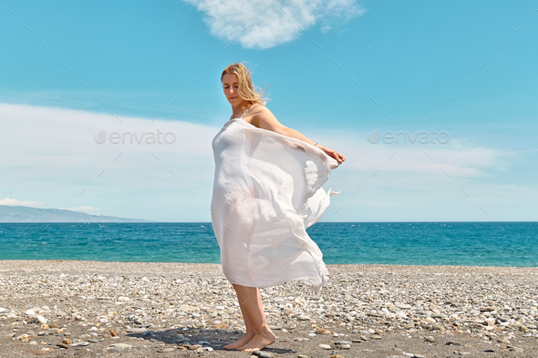 Pretty blond woman in swimsuit and white pareo enjoying sunny windy day ...