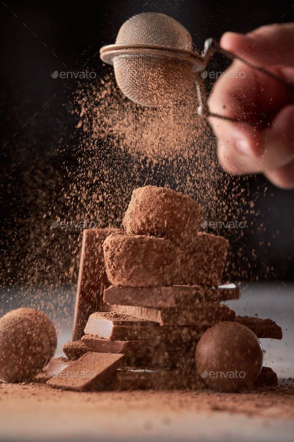 Hand sprinkles cocoa powder on chocolate candies. Stock Photo by wirestock