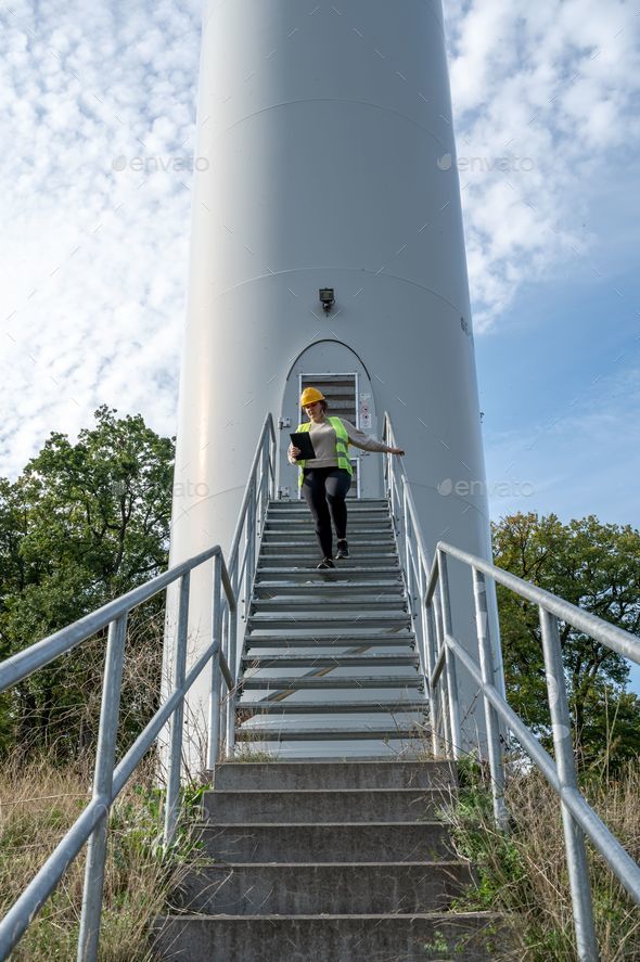 Woman engineer is making her way up down the stairs of a white windmill Stock Photo by wirestock