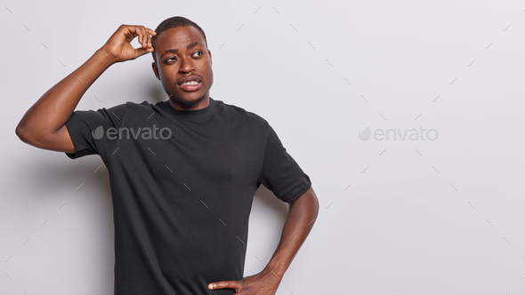 Thoughtful dark skinned man being deep in thoughts scratches head ...