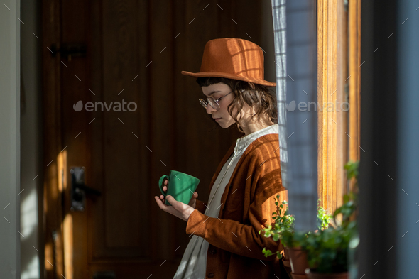 Sad depressed gen Z girl standing near window holding cup of tea ...