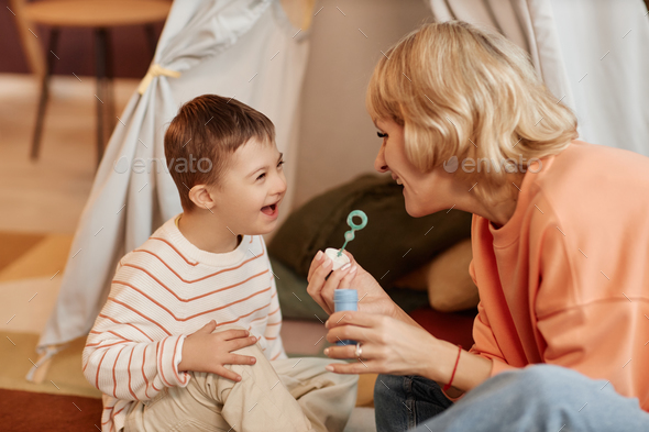 Boy with down syndrome blowing bubbles playing with mom Stock Photo by ...