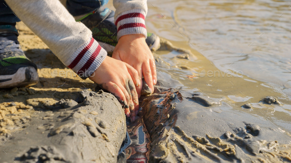 Closeup of little boy playing with wet sand on beach and digging a moat ...