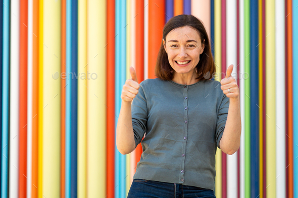 happy middle age woman against colorful background with thumbs up hand ...
