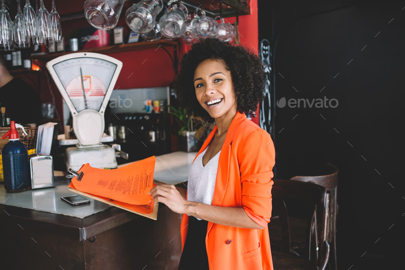 Cheerful young ethnic lady choosing food from menu standing near ...